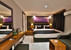 Quarto de hotel com duas camas, uma mesa, uma cadeira, um sofá, um espelho grande, um quadro, uma mesa de cabeceira, um abajur, um telefone e uma lixeira.