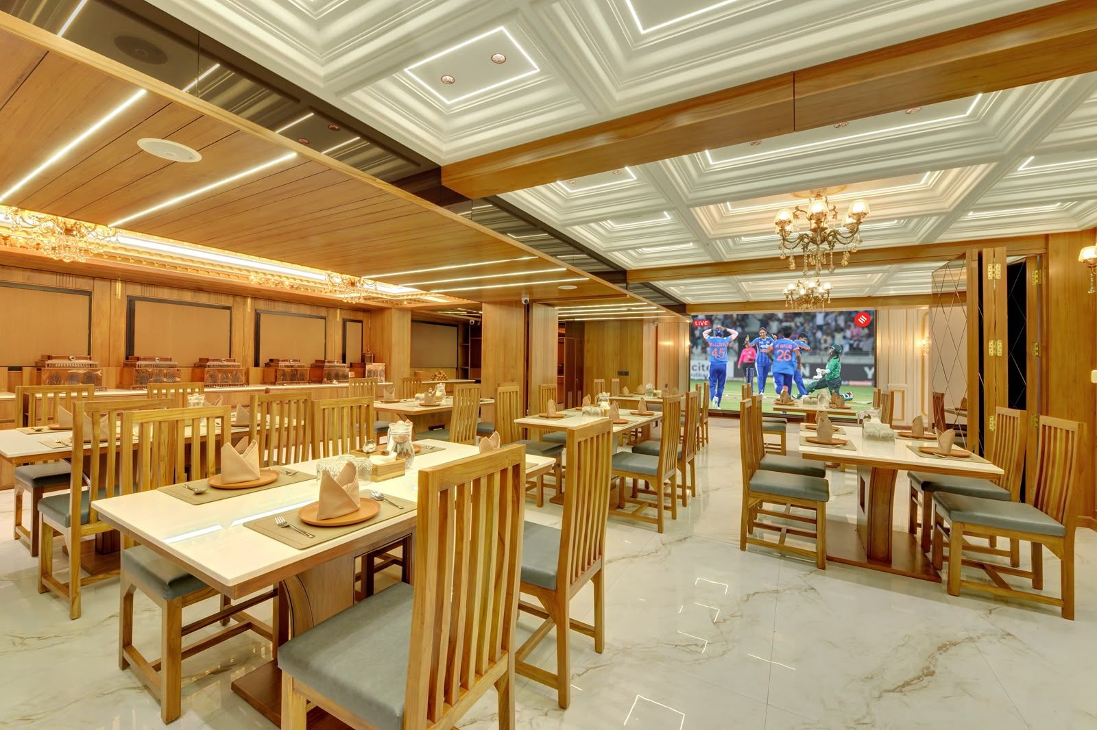 Restaurante com mobiliário de madeira, piso de mármore e teto com iluminação embutida.