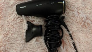 Secador de cabelo Philips Pro 2300W com cordão destacável e cabo de carregamento USB sobre uma superfície rosa e fofa.