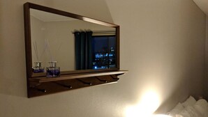 Quarto de hotel com um espelho grande, luminária de cabeceira e vista noturna da cidade.