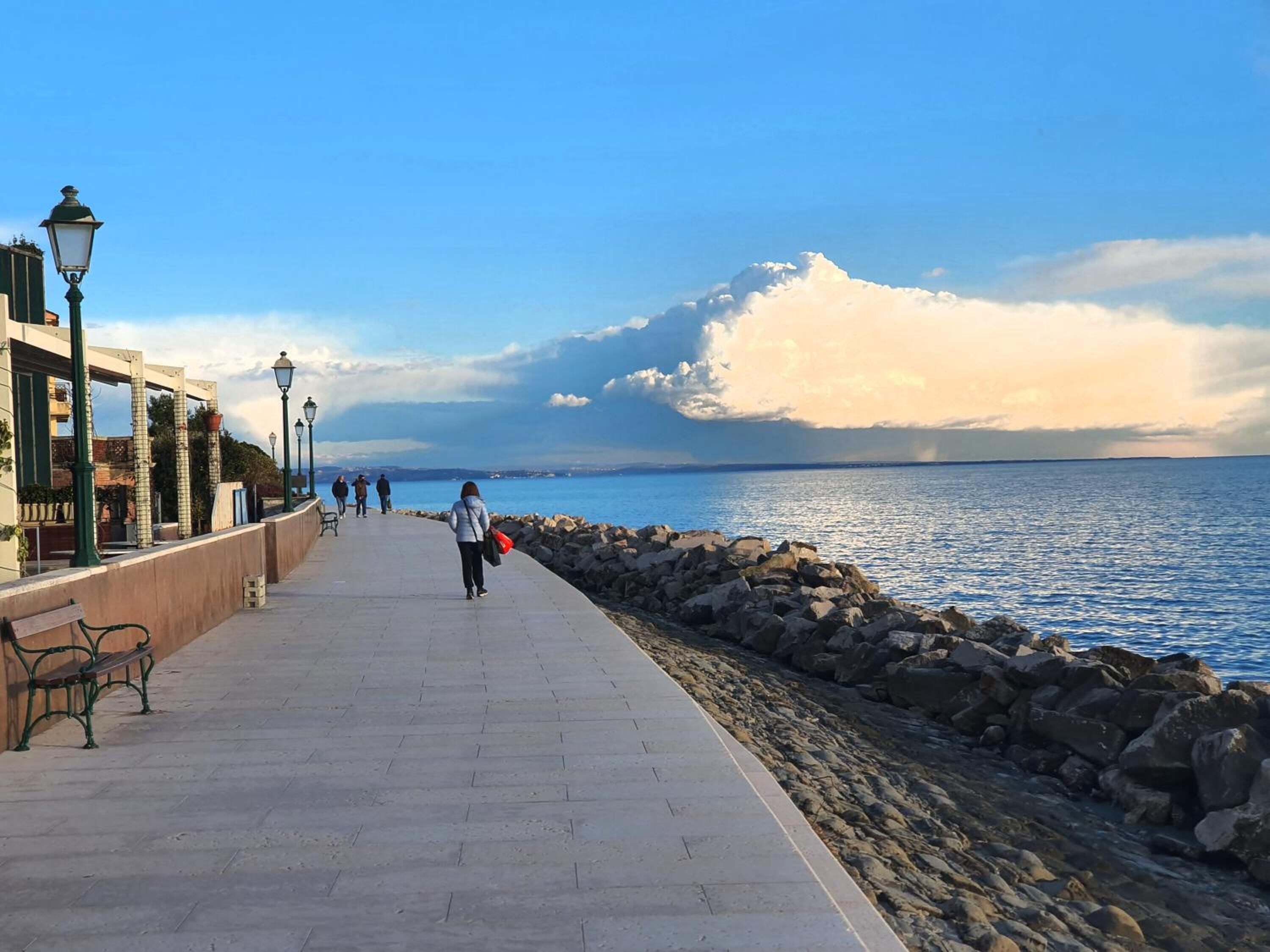 Uma orla costeira com calçada pavimentada, bancos e postes de iluminação.