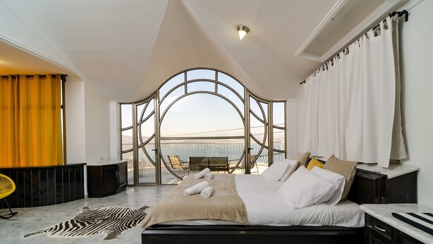 Quarto moderno com uma cama grande, vista da cidade e um design de janela em arco único.