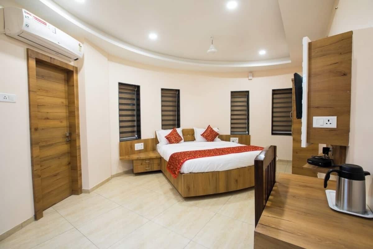 Quarto moderno com cama de madeira, mesa de cabeceira, cafeteira e televisão na parede.
