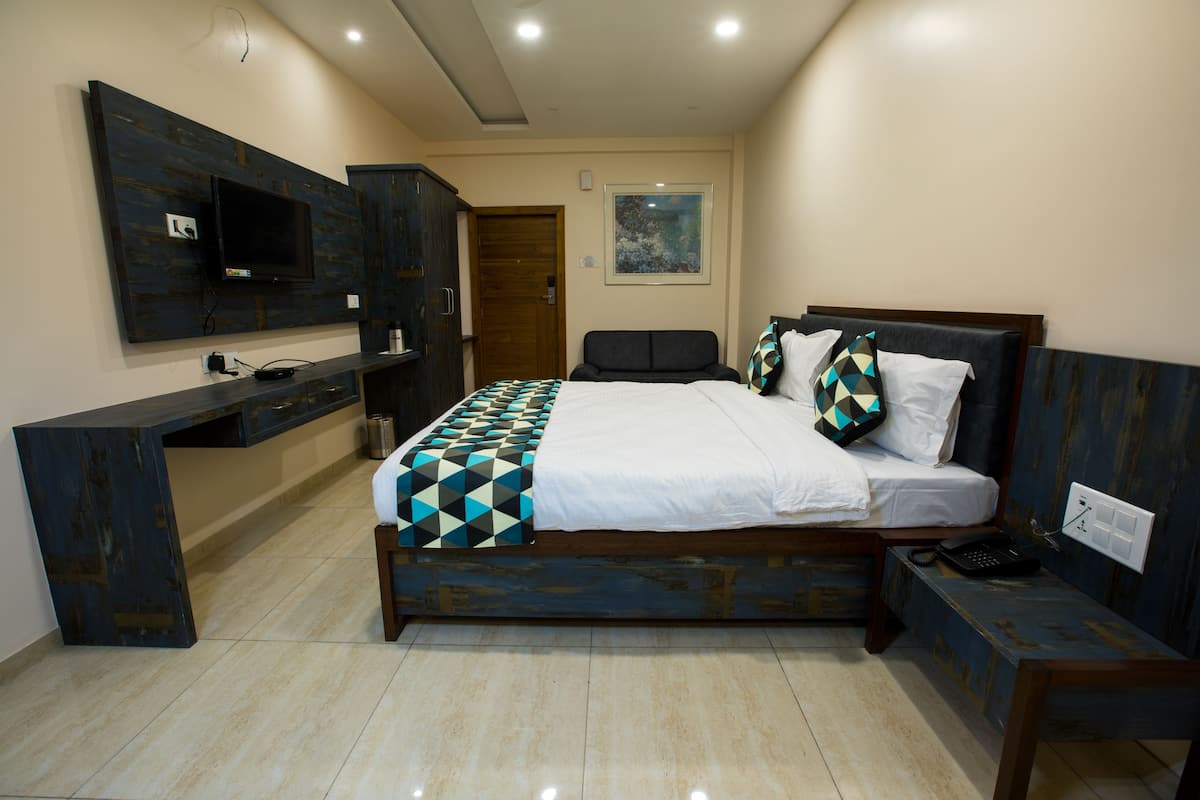 Quarto com cama, escrivaninha, televisão e um quadro na parede.