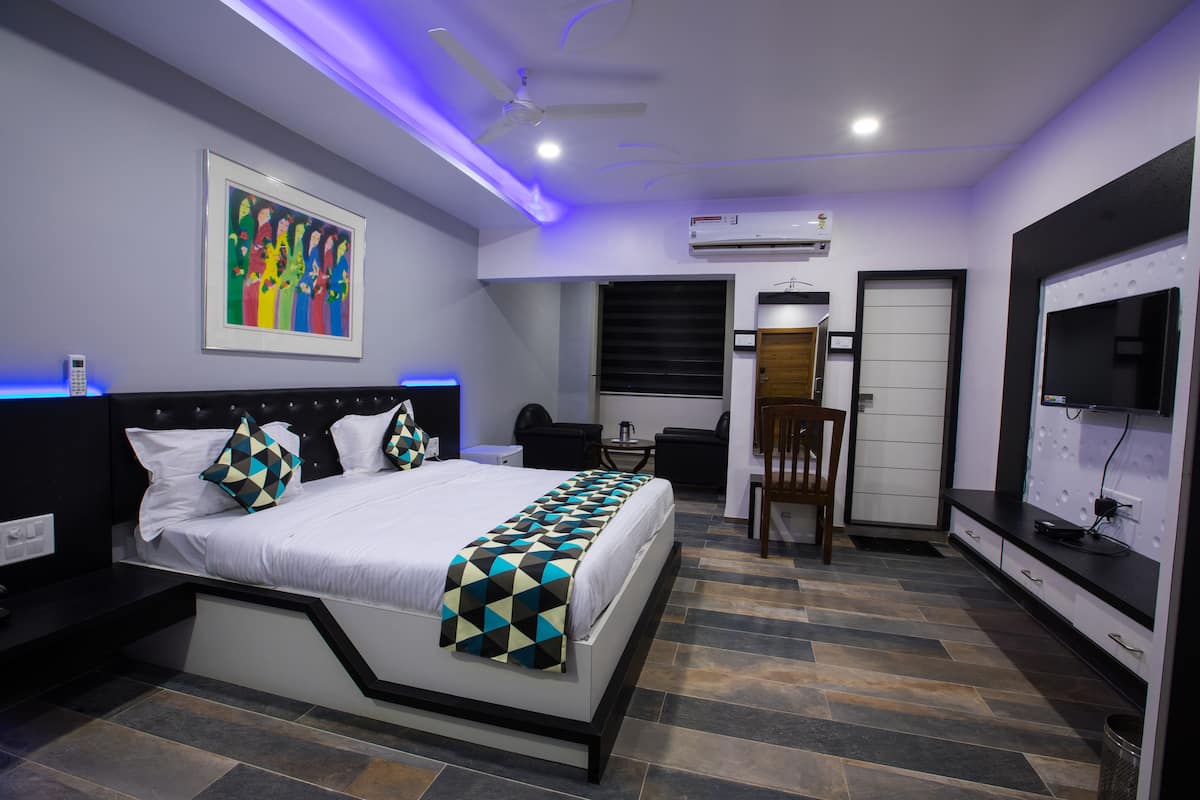 Quarto de hotel moderno com cama, escrivaninha, cadeira e televisão.