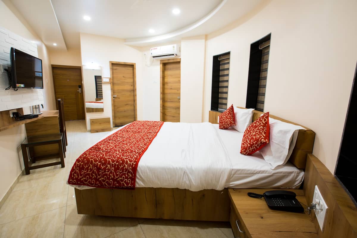 Quarto de hotel com cama, mesa de cabeceira, telefone, televisão e escrivaninha com cadeira.
