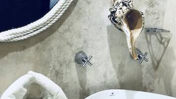 Casa de banho com espelho redondo, pia branca e concha decorativa na parede.