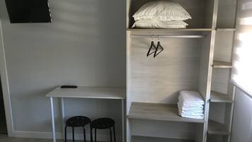 Quarto com cama, escrivaninha, duas cadeiras, televisão e guarda-roupa.