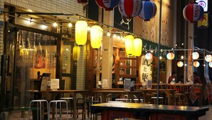 Restaurante com mesas ao ar livre, lanternas tradicionais e sinalização japonesa.
