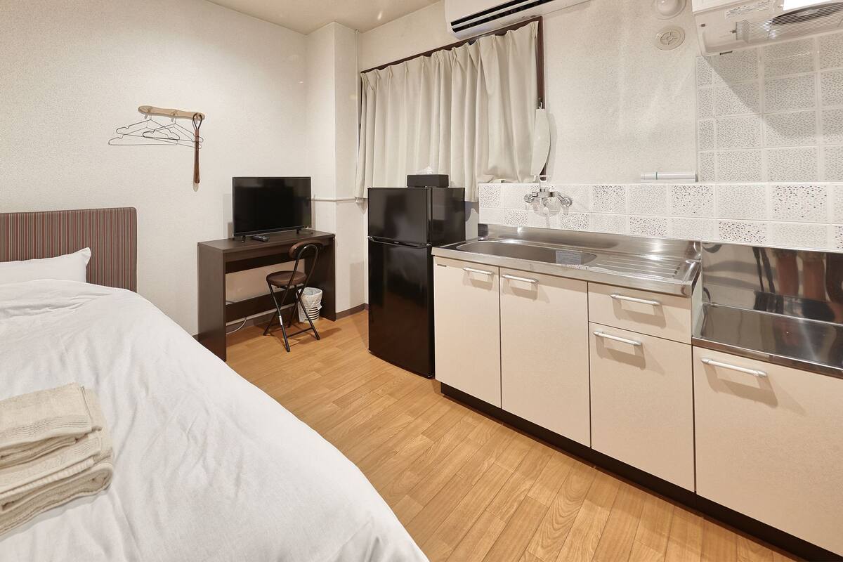 Quarto de hotel com cama, televisão, frigorífico, pia e pequena secretária.