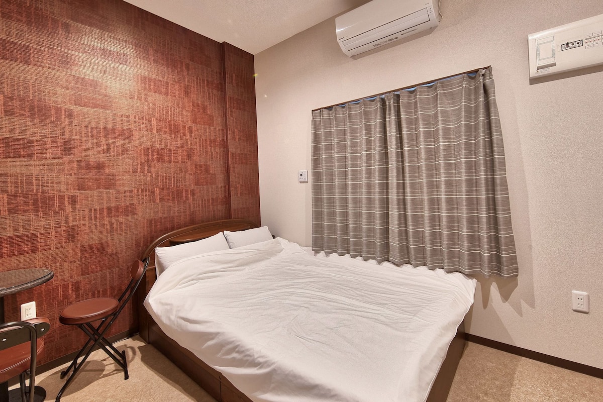 Quarto de hotel com uma cama, uma mesa pequena, uma cadeira, uma televisão e ar condicionado.