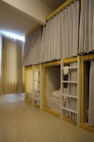 Quarto de hotel com beliches, cortinas e piso ladrilhado.