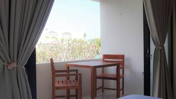 Quarto de hotel com cama, mesa, duas cadeiras e varanda com cortinas.