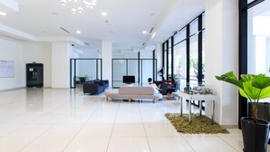 Um hall amplo com design moderno, apresentando uma grande área de estar, um balcão de recepção e grandes janelas que oferecem luz natural.