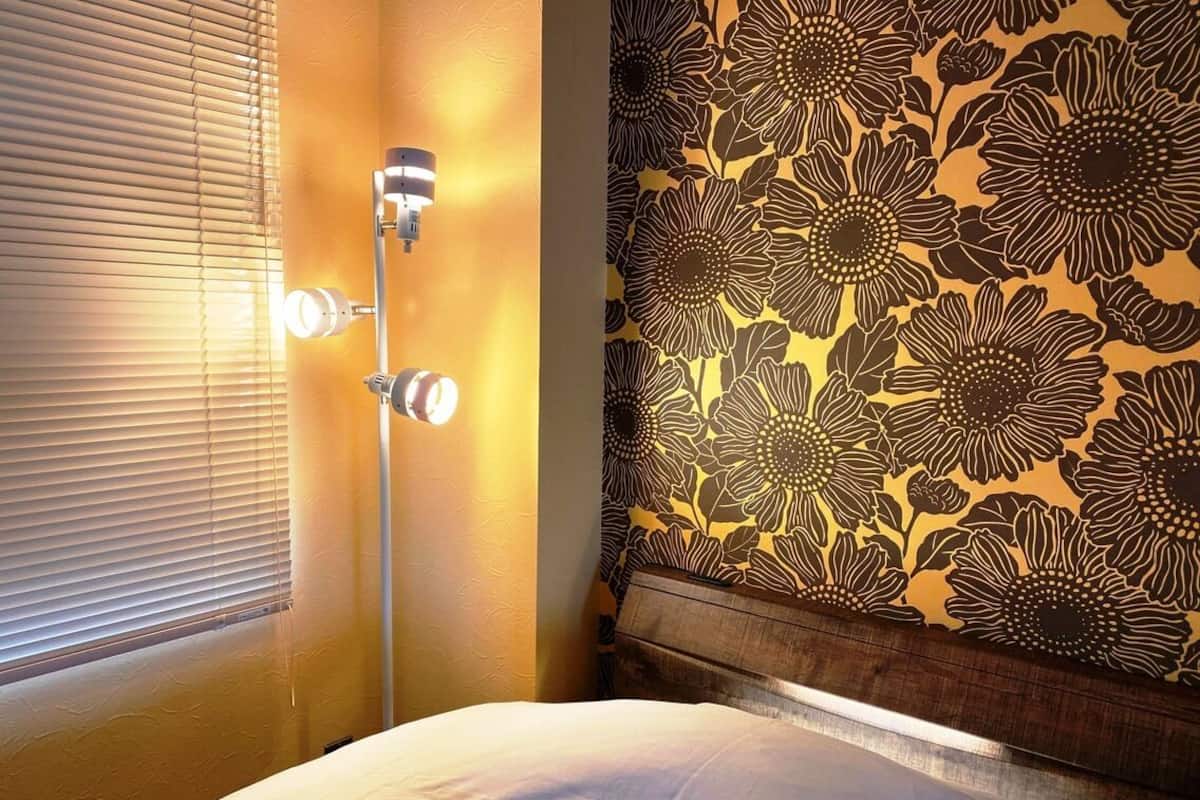 Quarto com cama, luminária na parede e papel de parede com padrão floral.
