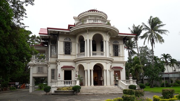 Um edifício grande e branco em estilo colonial, com fachada simétrica, várias varandas e uma entrada central.