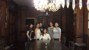 Um grupo de pessoas sentado ao redor de uma mesa redonda em uma sala com painéis de madeira e um candelabro.
