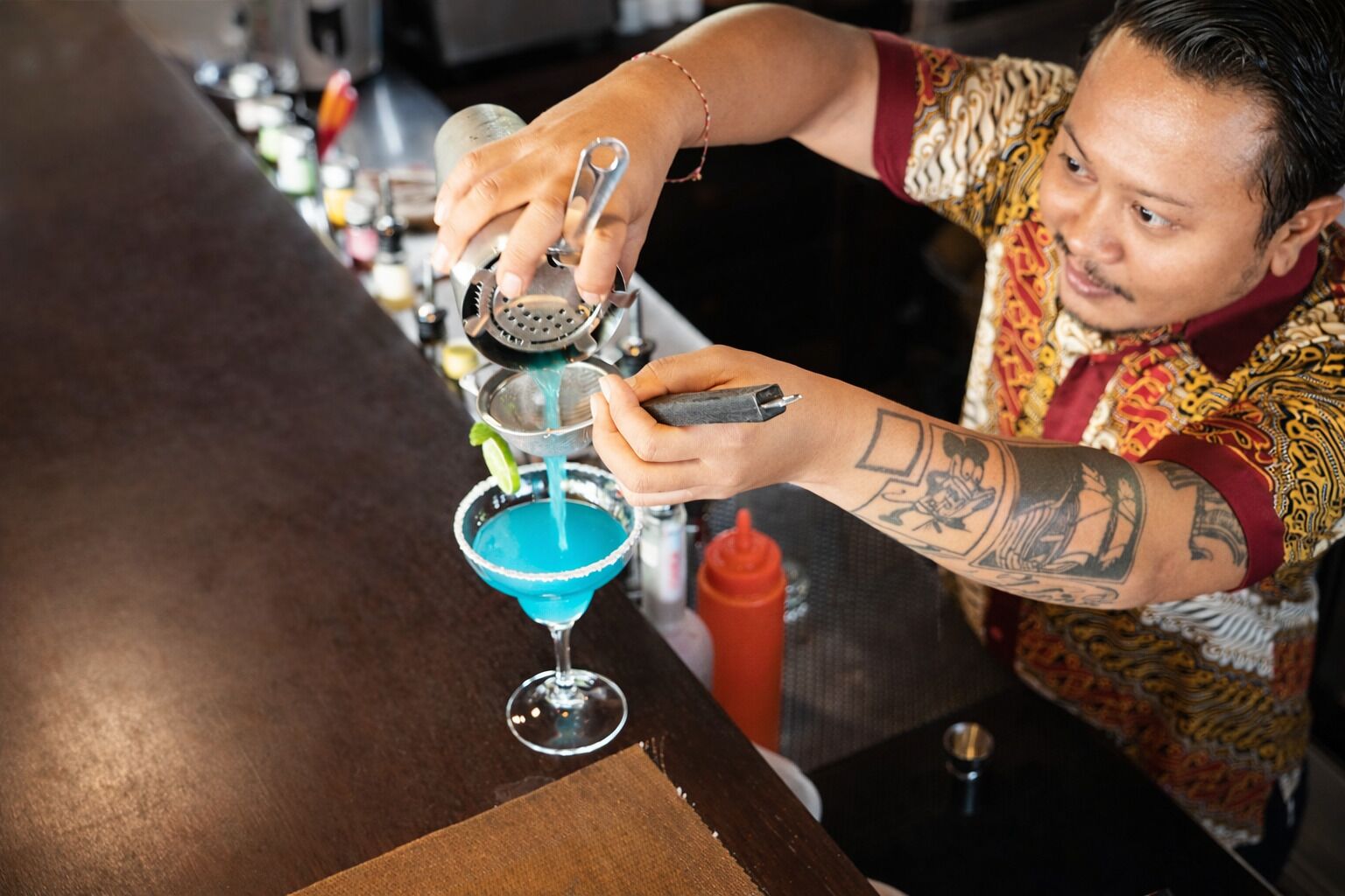 Um bartender preparando um coquetel azul com uma fatia de limão.