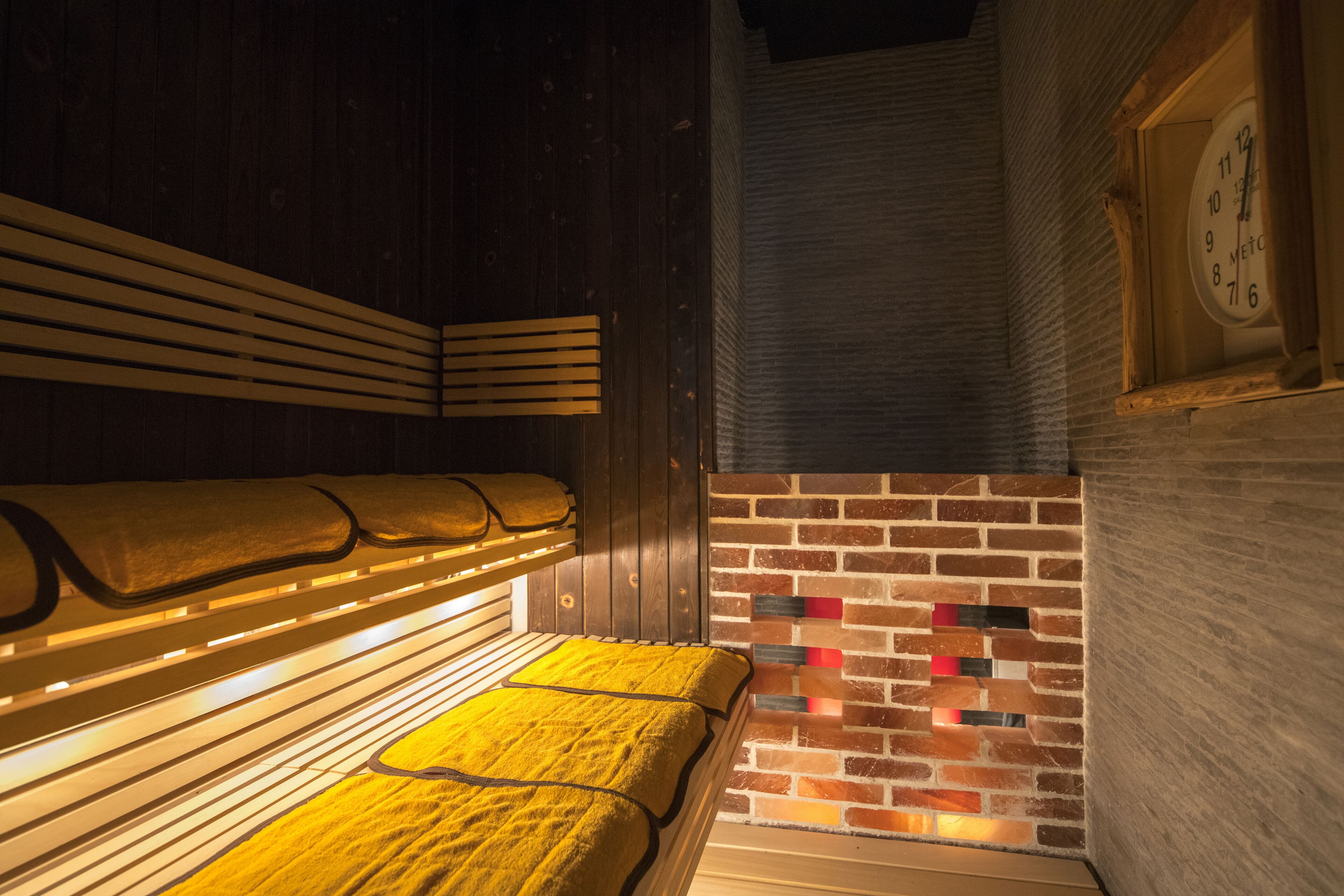 Um quarto com uma cama de ripas de madeira, parede de tijolos e um relógio.