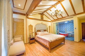 Quarto com cama de madeira, mesa de cabeceira, cadeira e uma janela grande com vista para uma banheira vermelha.
