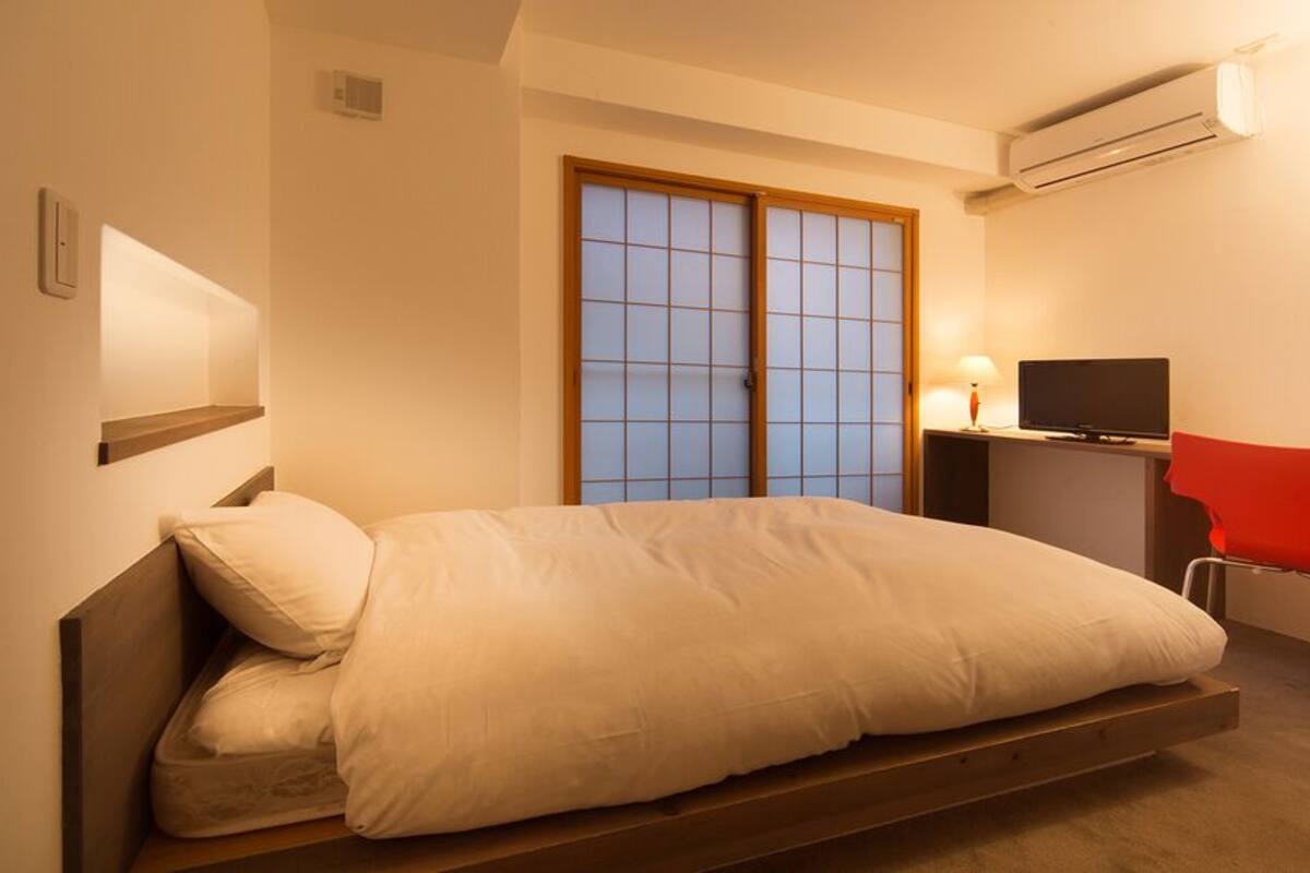 Quarto com cama, televisão, cadeira e janela com vista.