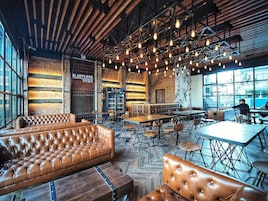 Um café espaçoso, com assentos de couro, paredes de tijolo aparente e teto alto com luminárias pendentes.