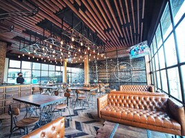 Um café espaçoso com pé-direito alto, vigas aparentes e grandes janelas que oferecem vista da cidade.