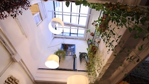 Visão do interior de um edifício com pé-alto, grandes janelas e plantas penduradas.