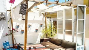 Um pátio externo acolhedor com um sofá marrom, cadeiras azuis e uma mesa com um tapete colorido.
