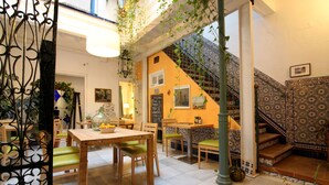 Uma área de refeições com mesa e cadeiras de madeira, escada com azulejos estampados e plantas penduradas.