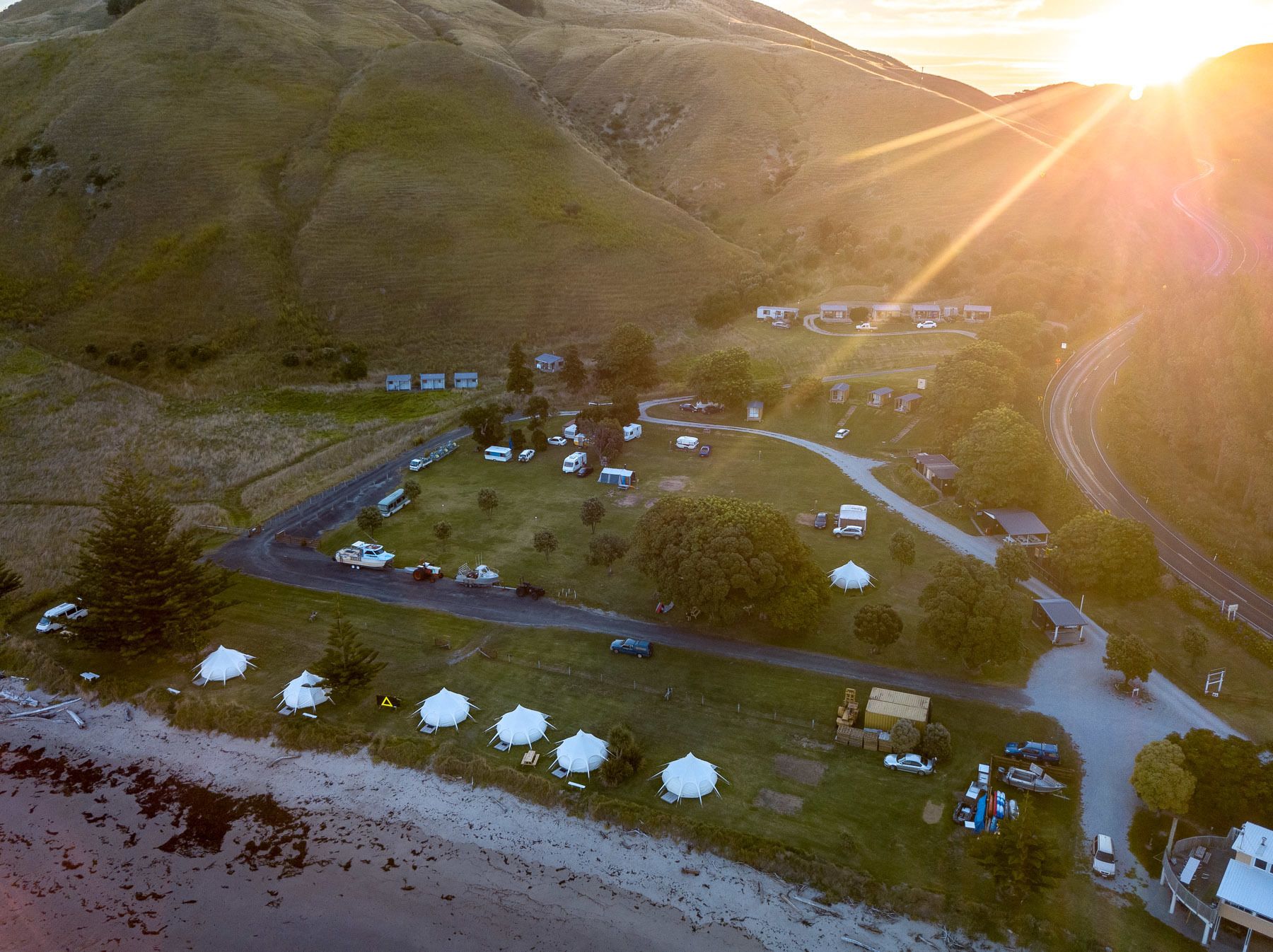 Vista aérea de um camping com tendas, trailers e uma estrada sinuosa.