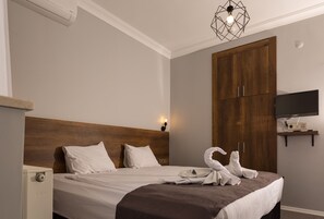 Cama bem arrumada com roupa de cama branca, cabeceira de madeira e uma televisão de tela plana em uma prateleira acima.