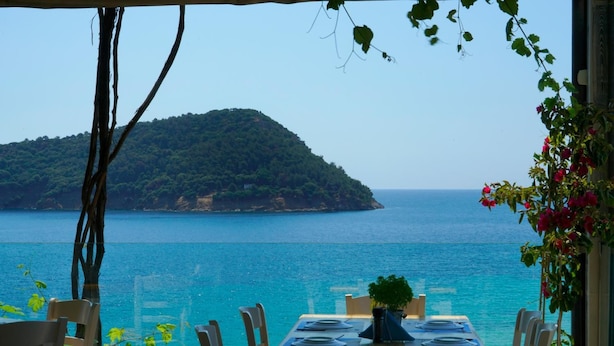 Mesa posta para refeição, com vista para um mar calmo e uma ilha verde ao longe.