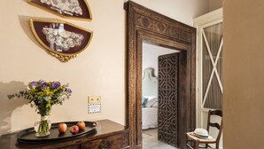 Uma cômoda de madeira com um vaso de flores e maçãs, um espelho com renda, e uma porta estampada.