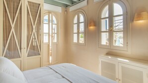 Quarto com cama, guarda-roupa e janelas em arco com cortinas.