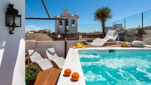 Uma área de piscina no terraço com espreguiçadeiras, um campanário e uma palmeira.