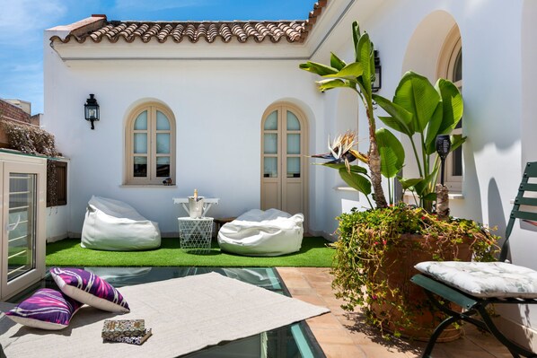 Um edifício branco com duas janelas em arco, uma piscina pequena e área de estar ao ar livre.