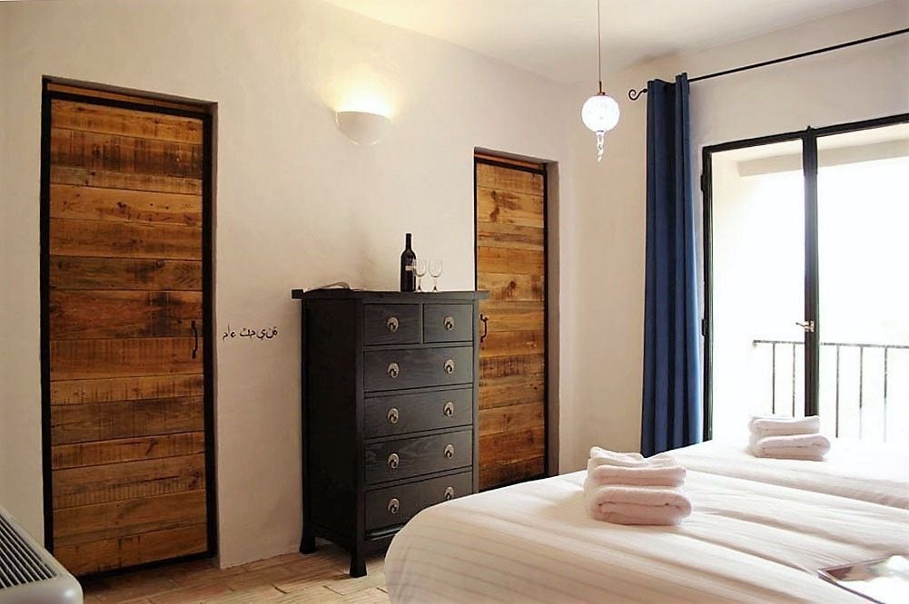 Quarto de hotel com guarda-roupa de madeira, penteadeira, cama com toalhas e vista para varanda.