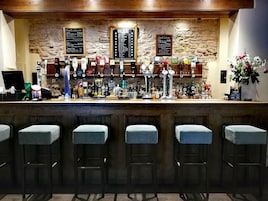 Uma área de bar com parede de pedra, várias torneiras e um quadro de cardápio.