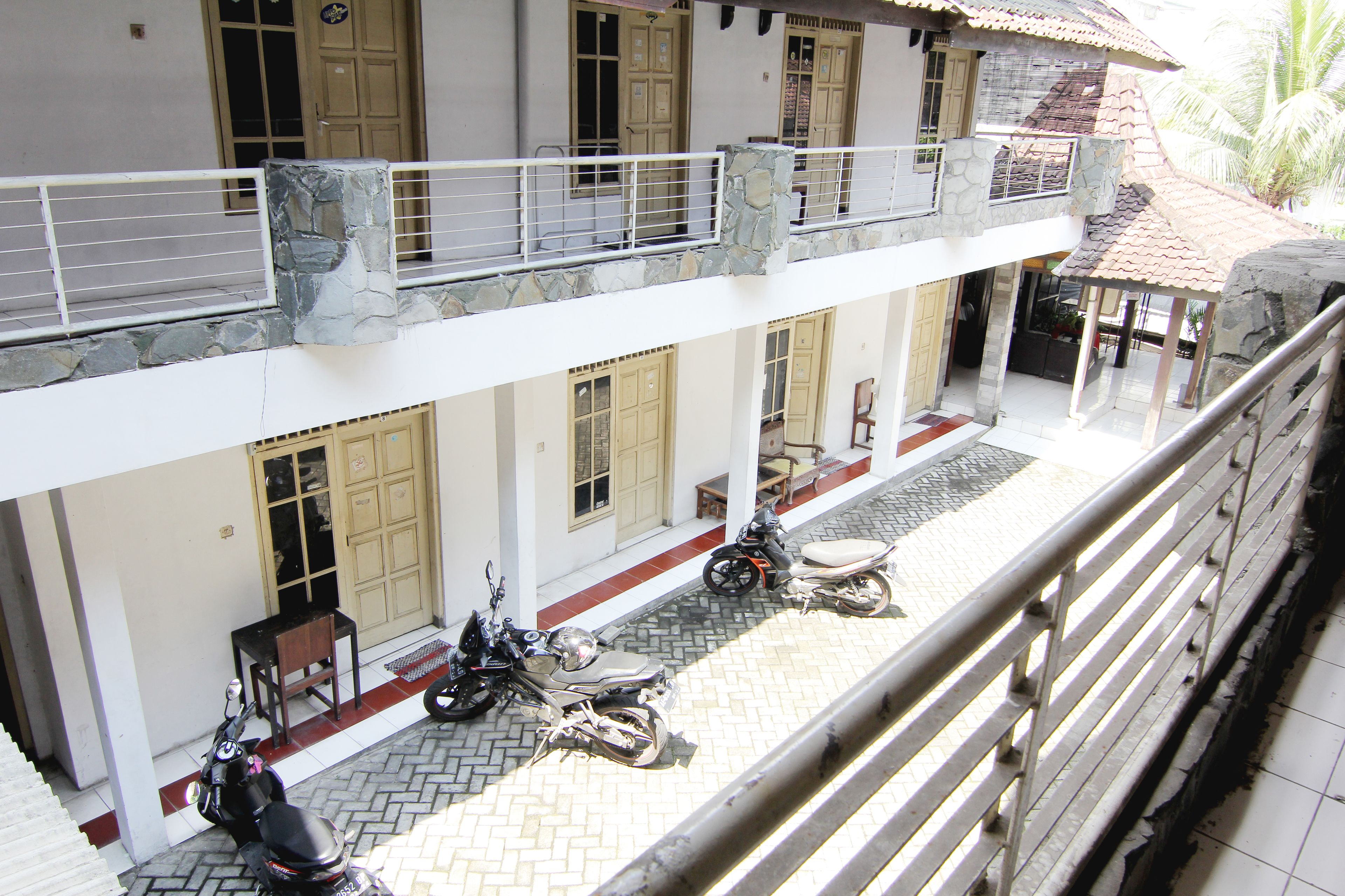 Um edifício de dois andares com varanda, piso de azulejos e uma fileira de motocicletas estacionadas.