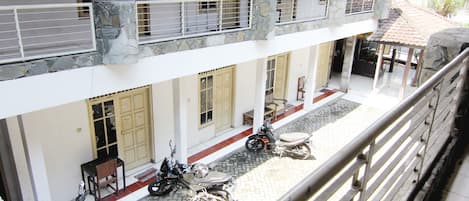 Um edifício de dois andares com varanda, piso de azulejos e uma fileira de motocicletas estacionadas.
