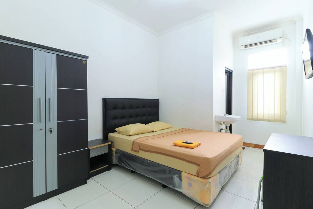 Quarto com cama, guarda-roupa, mesa de cabeceira, abajur e janela com persianas.