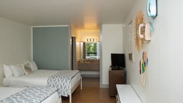 Quarto de hotel com duas camas, televisão, escrivaninha, banheiro com pia e espelho, e telefone na parede.