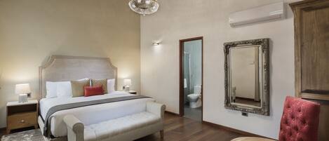 Quarto com uma cama grande, mesas de cabeceira, um lustre, um espelho e piso de madeira.