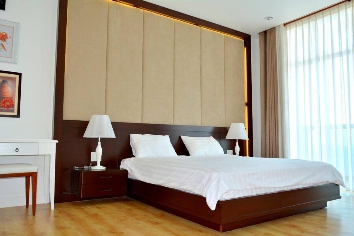 Quarto de hotel com uma cama grande, duas mesas de cabeceira com luminárias, uma escrivaninha e uma cadeira.