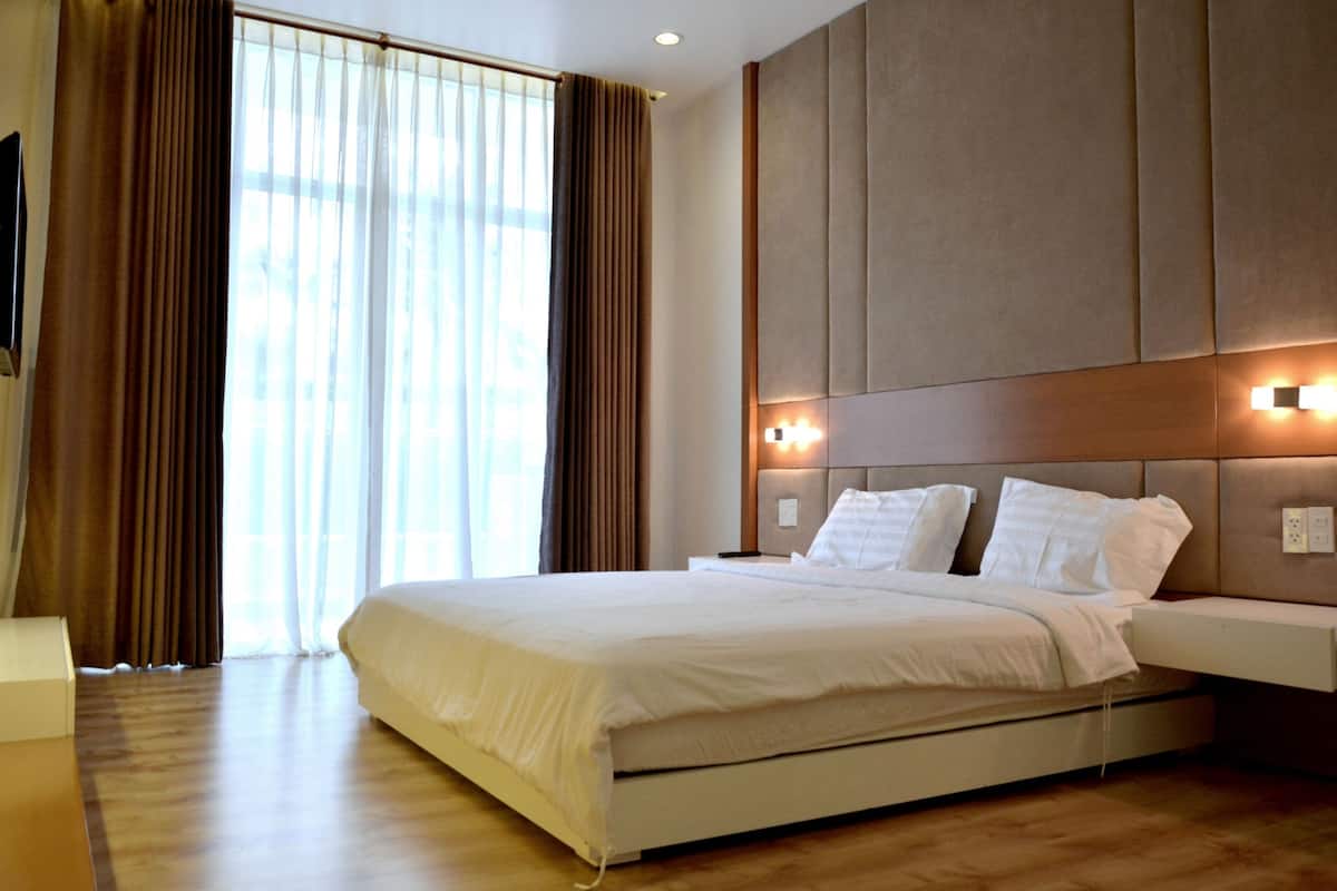 Quarto de hotel moderno com uma cama grande, mesa de cabeceira e luminária fixada na parede.