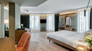 Quarto de hotel moderno com uma cama grande, uma escrivaninha com cadeira, um guarda-roupa e uma televisão fixada na parede.