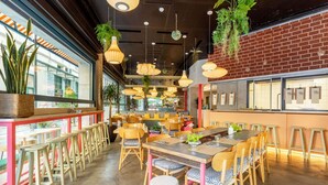 Um restaurante com mesas altas e banquetas, plantas penduradas e parede de tijolos.
