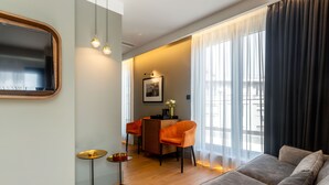 Uma sala de estar moderna com um sofá cinzento, uma mesa de centro de madeira e um espaço de jantar com cadeiras laranja e uma pequena mesa.