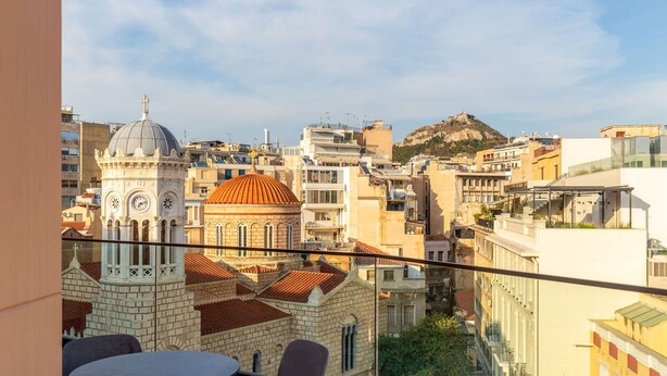 Varanda com mesa e cadeiras, vista para um horizonte urbano com edifícios históricos e uma colina ao fundo.